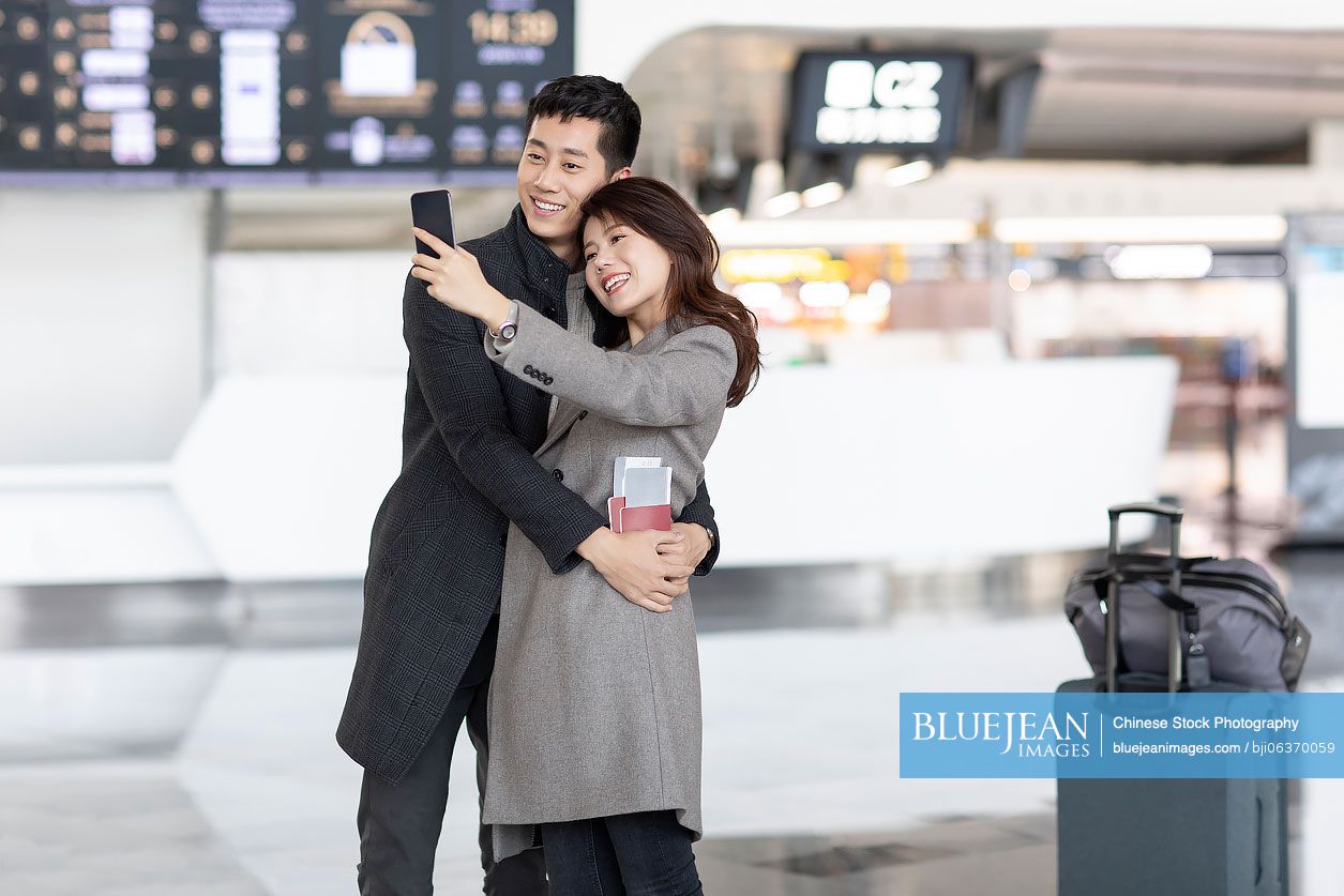 Happy young Chinese couple using smartphone at the airport-High-res stock photo for download