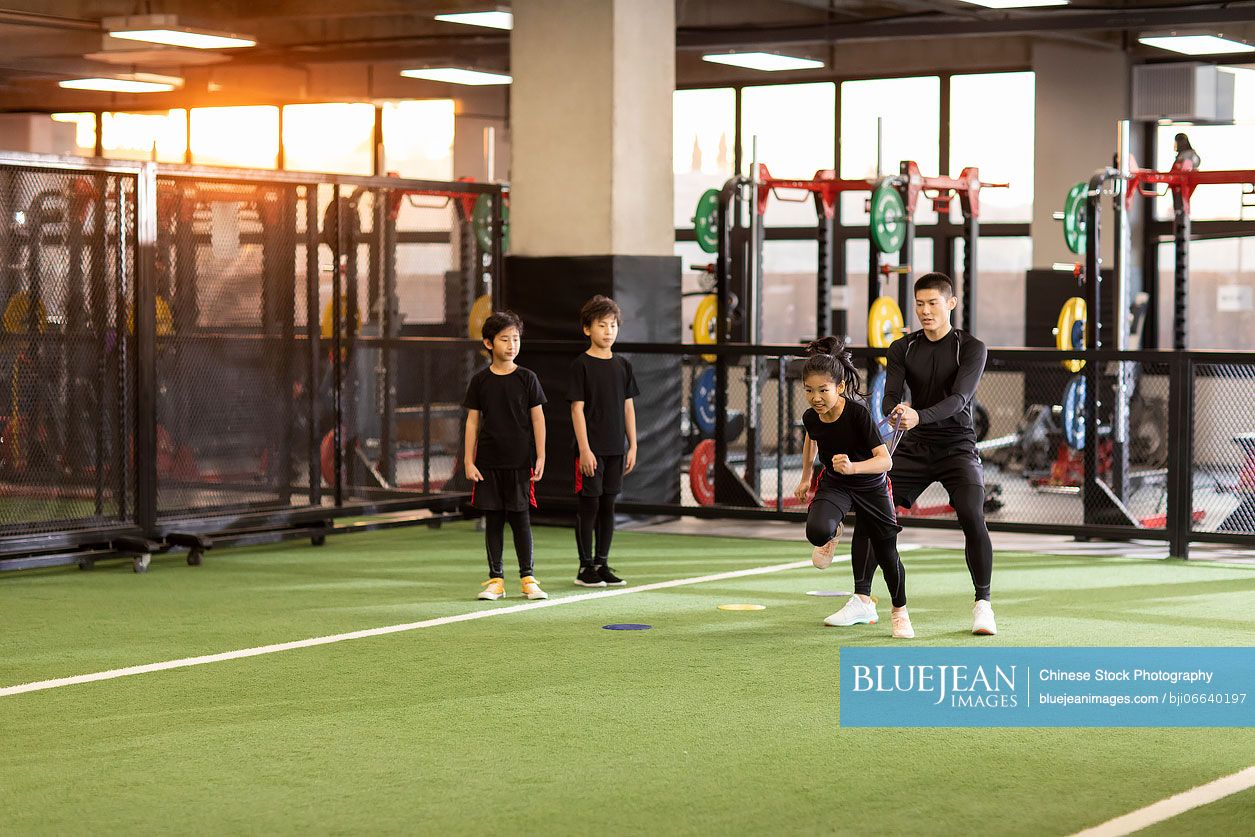 Active Chinese children having exercise class with their coach in gym ...