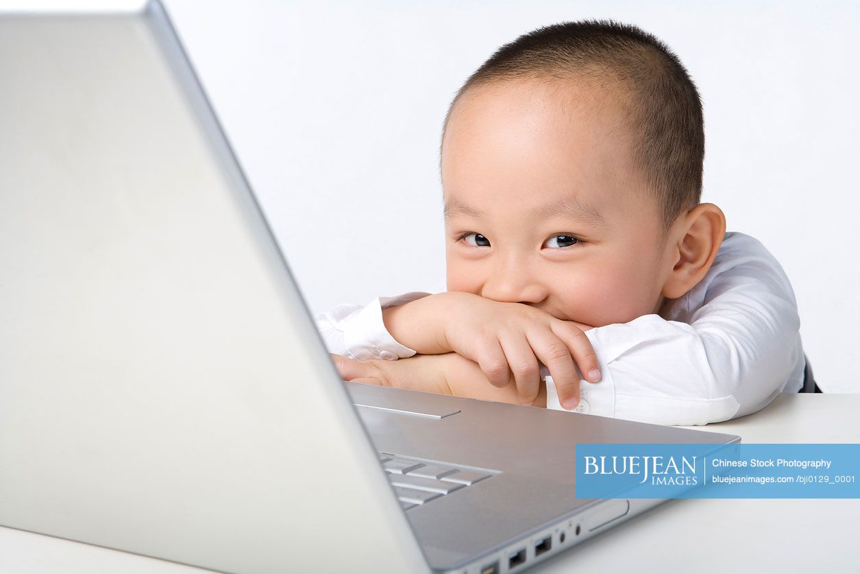 Young Chinese boy sits at a laptop and smiles-High-res stock photo for ...