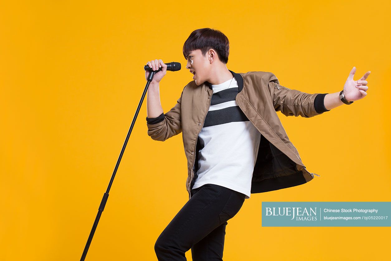 Cheerful young Chinese man singing with microphone-High-res stock photo for download