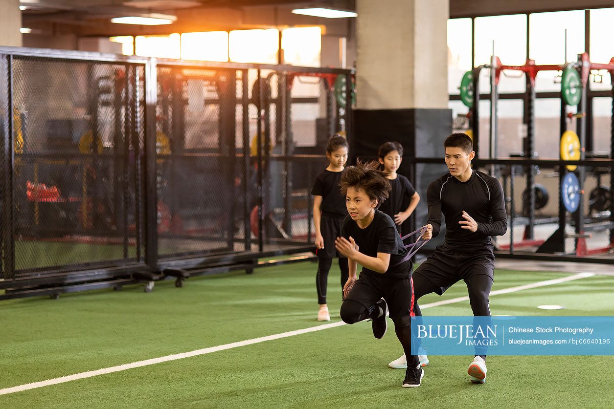 Active Chinese children having exercise class with their coach in gym ...
