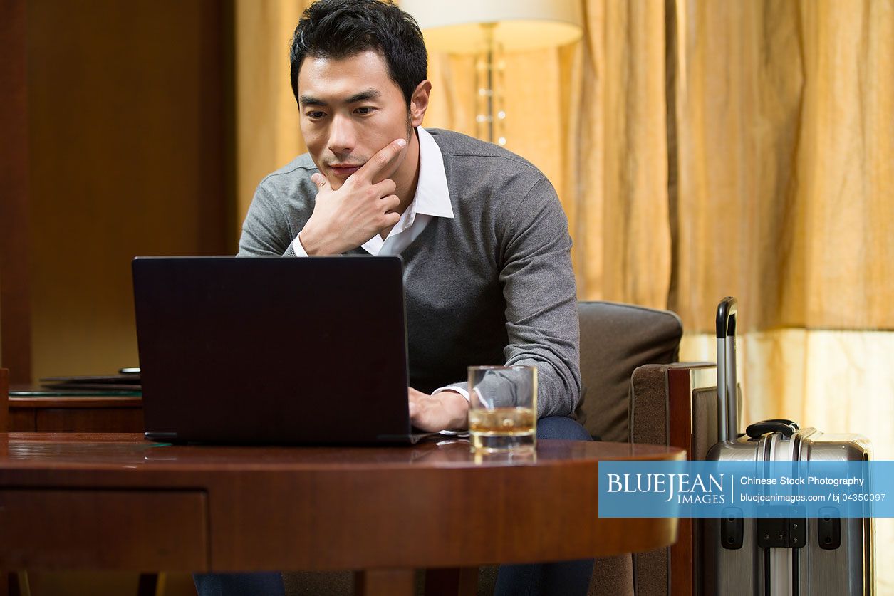 Young Chinese businessman using laptop in hotel room-High-res stock photo for download