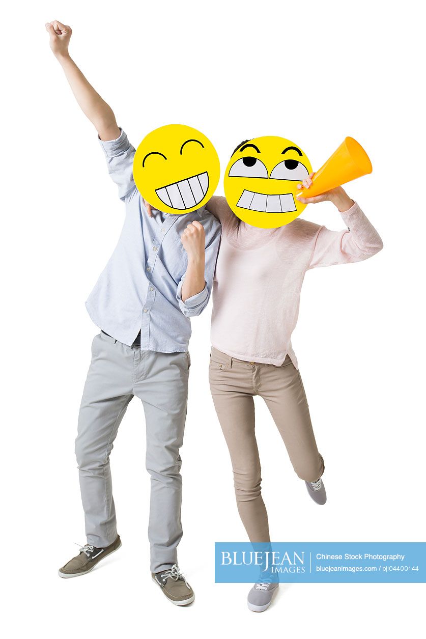 Young Chinese couple cheering with two happy emoticon faces in front of ...