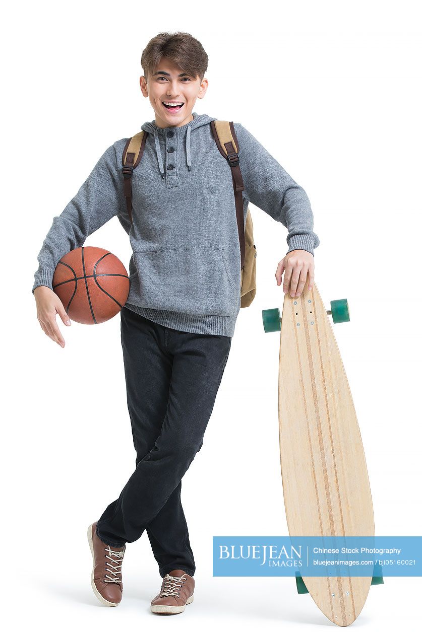 Cheerful male college student holding skateboard and basketball-High ...