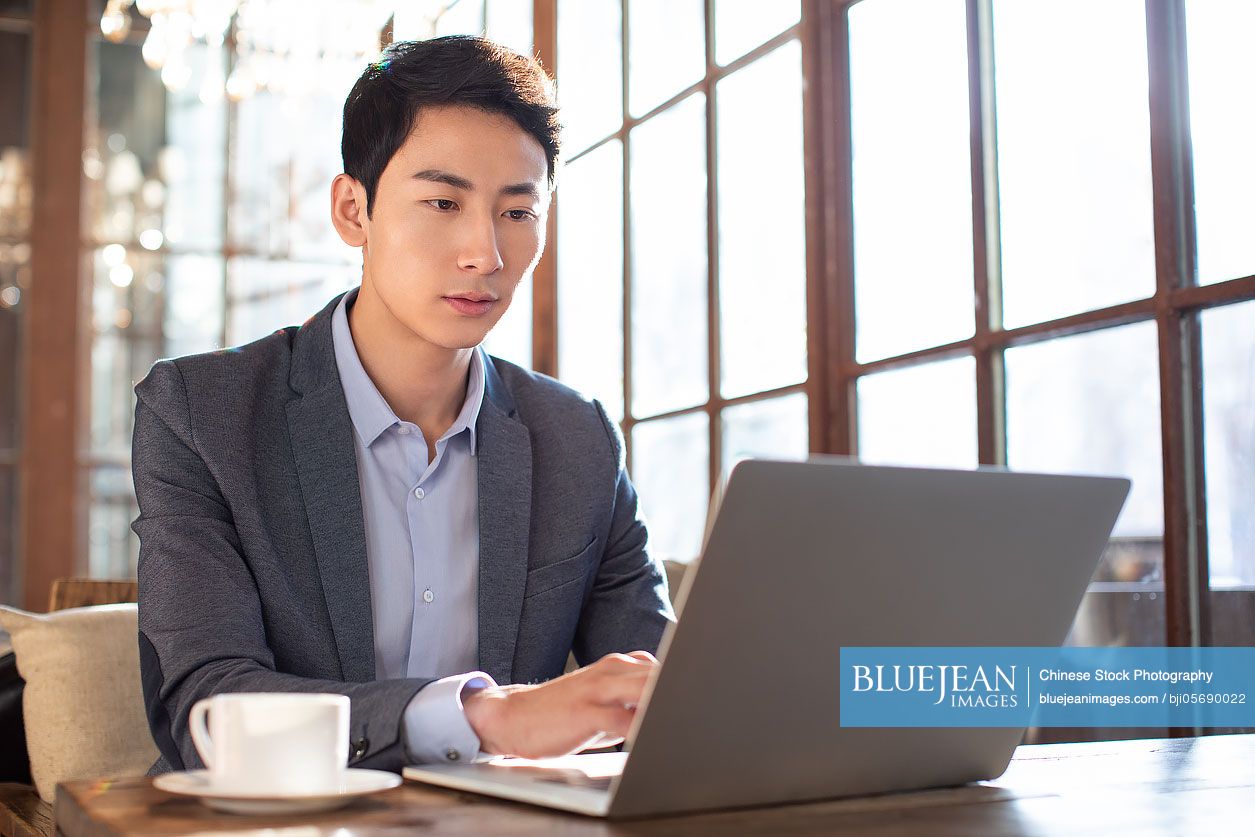 Young Chinese businessman using laptop in coffee shop-High-res stock photo for download