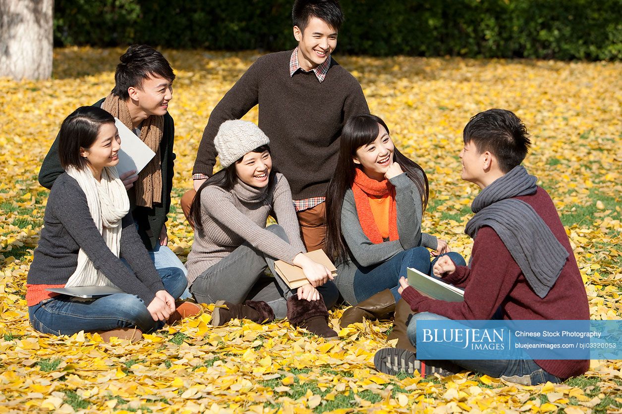 Happy Chinese college students sharing stories on campus in a beautiful ...