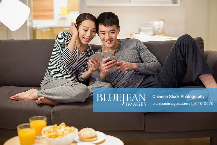 Young Chinese couple using smart phones on living room sofa-High-res ...