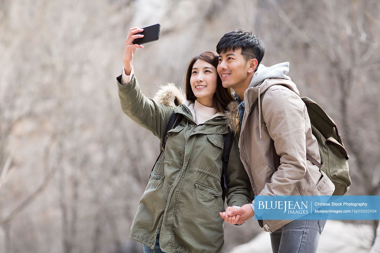 Happy young Chinese couple taking selfies outdoors in winter-High-res stock photo for download