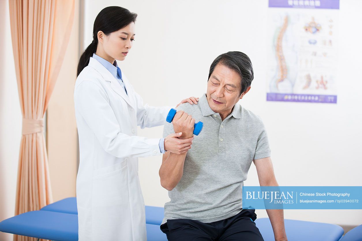Senior Chinese patient exercising with dumbbell under doctor's help ...