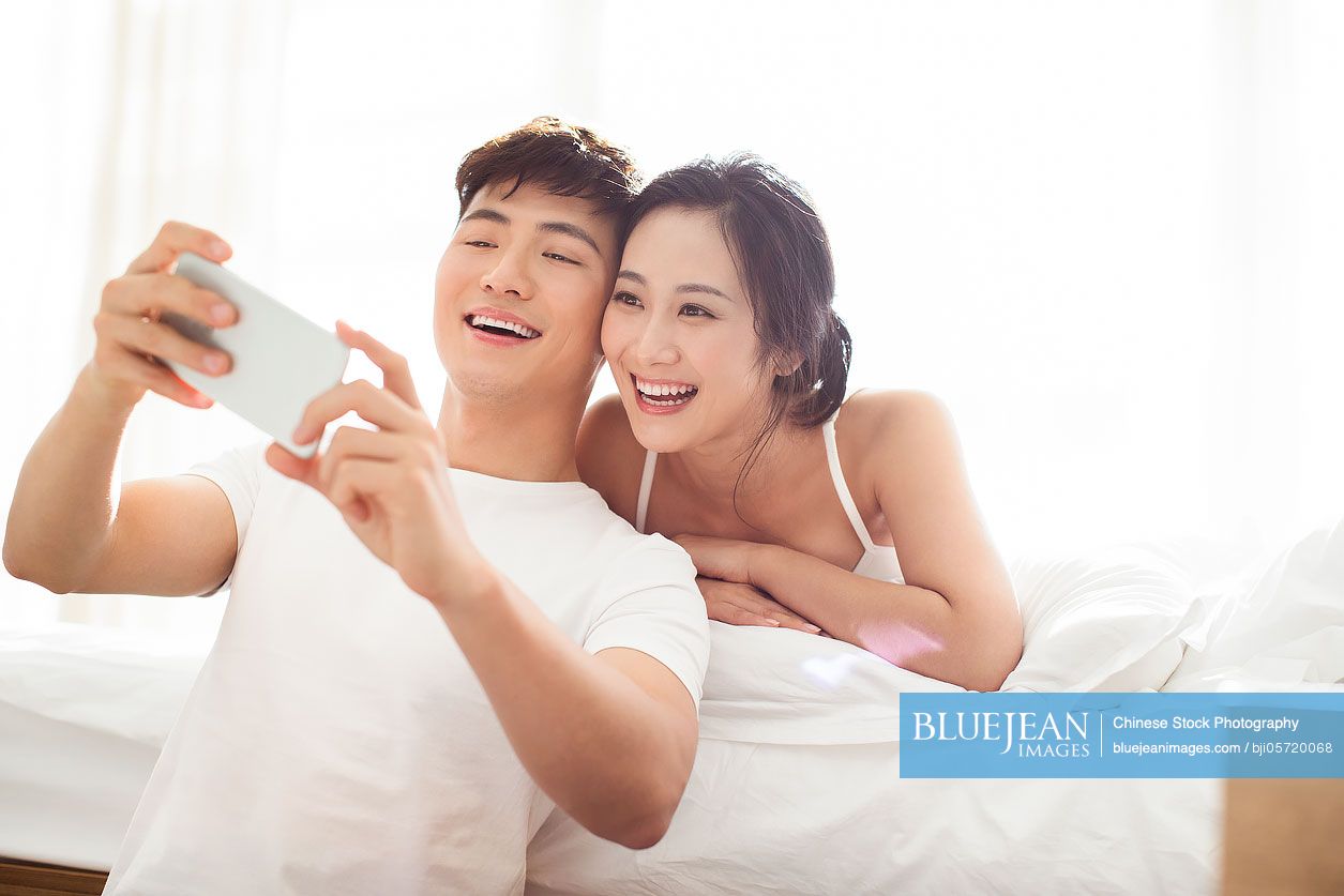 Happy young Chinese couple using smartphone in bedroom-High-res stock ...