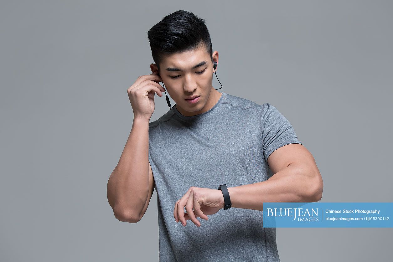 Young Chinese male athlete with headphones checking smart watch after ...