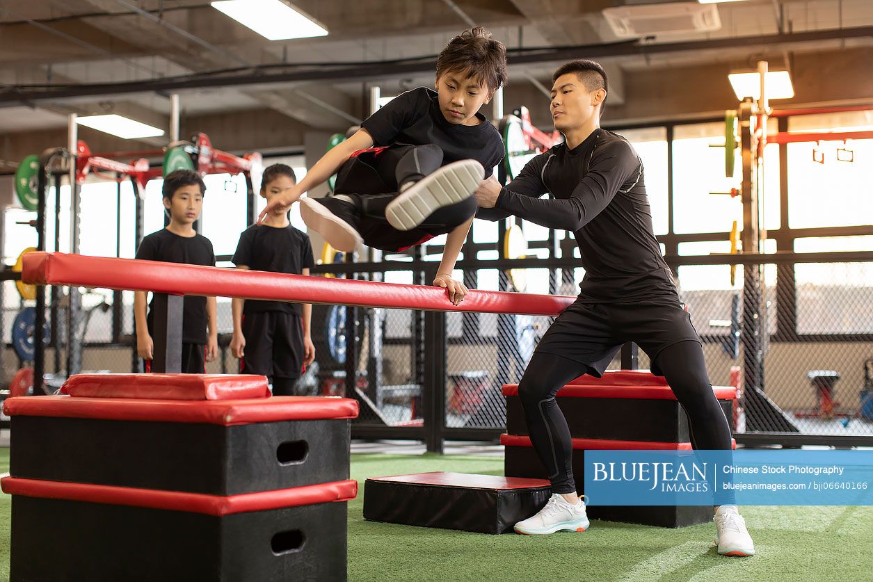 Active Chinese children having exercise class with their coach in gym ...