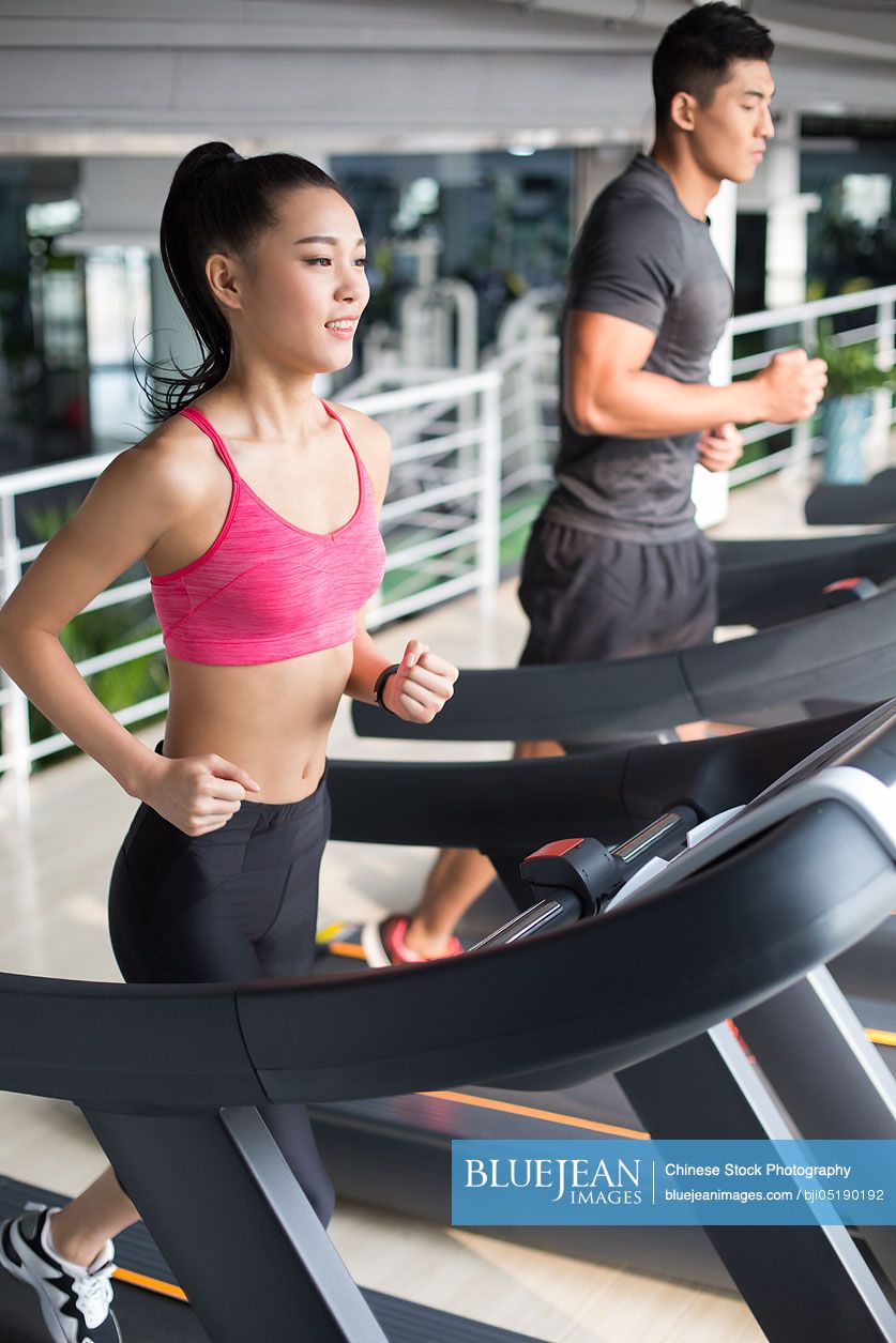 Young Chinese couple running on treadmills in gym-High-res stock photo for download
