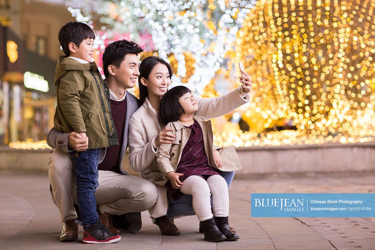 Cheerful young Chinese family taking self portrait with smart phone ...
