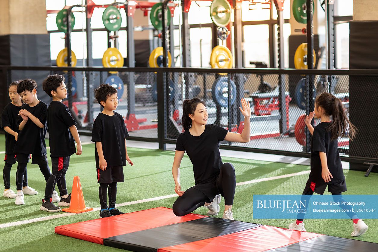 Active Chinese children having exercise class with their coach in gym ...