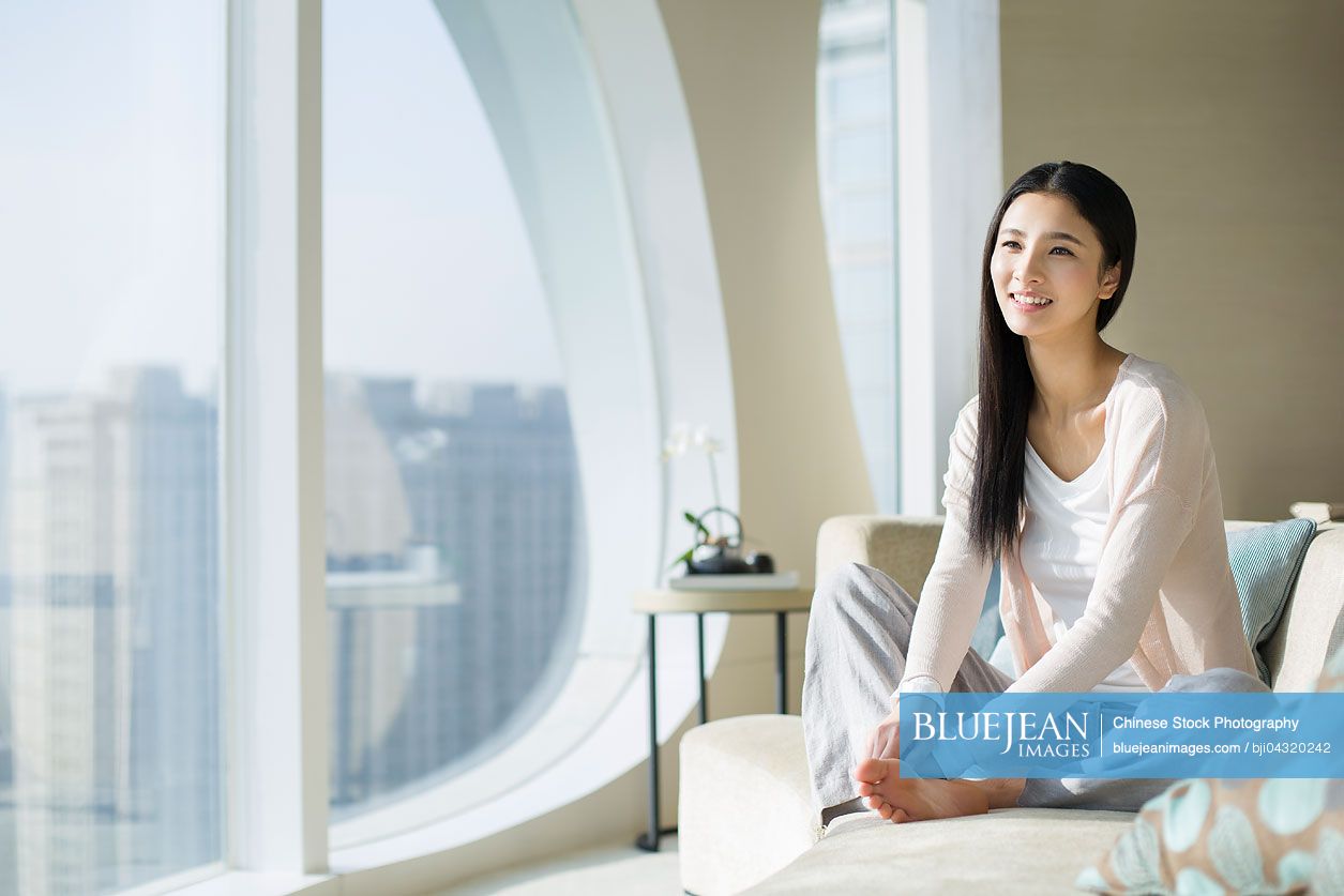 Happy young Chinese woman sitting by window-High-res stock photo for download