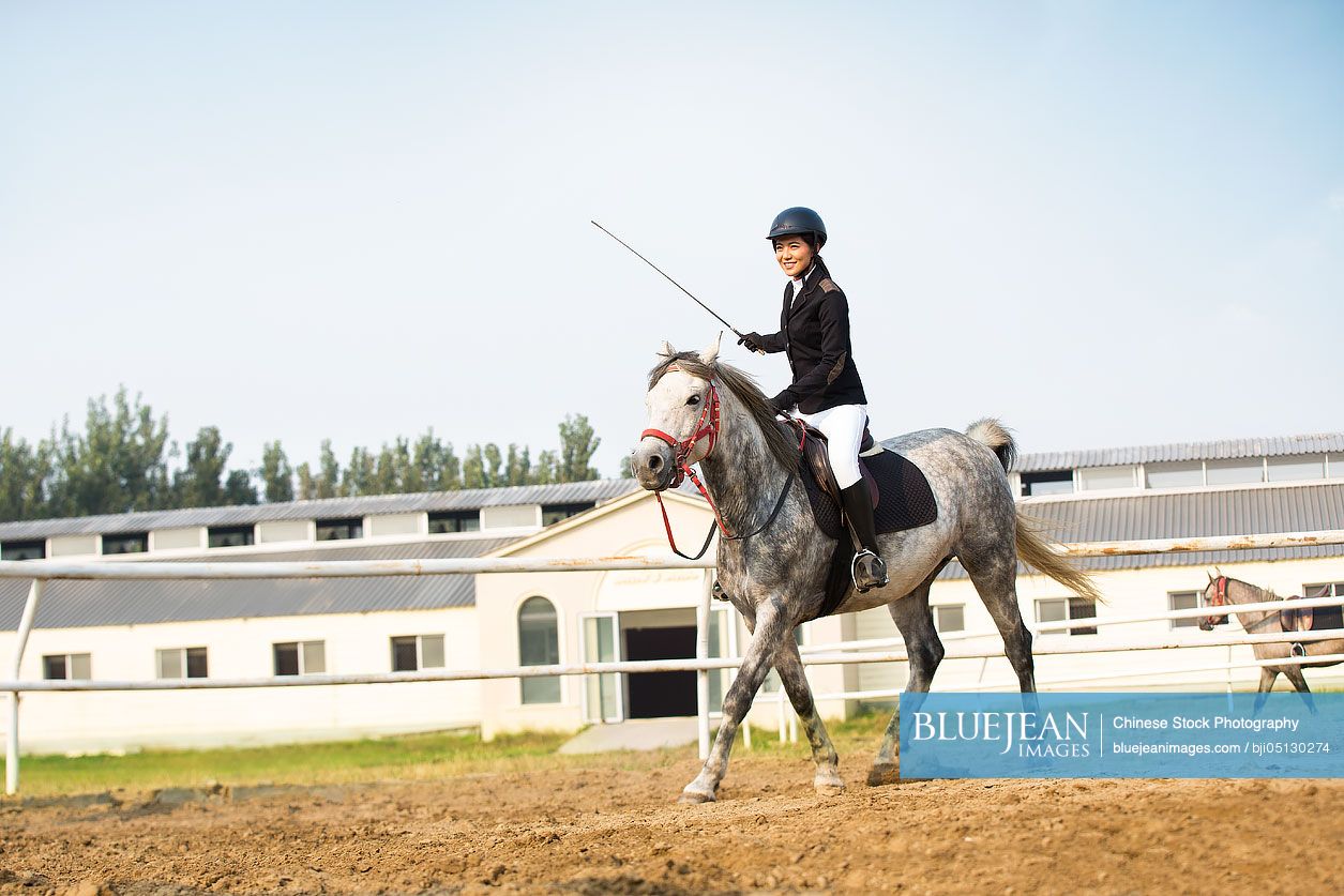 Cheerful young Chinese woman riding horse-High-res stock photo for download