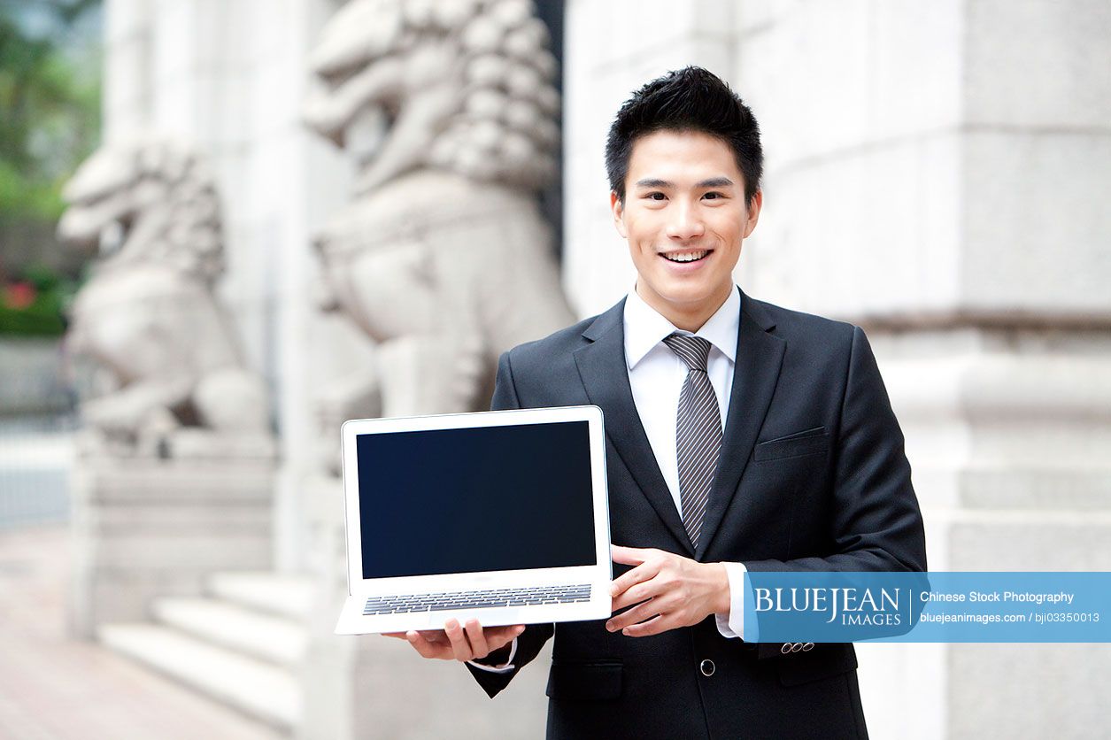 Happy young Chinese businessman with a laptop outdoors, Hong Kong-High-res stock photo for download