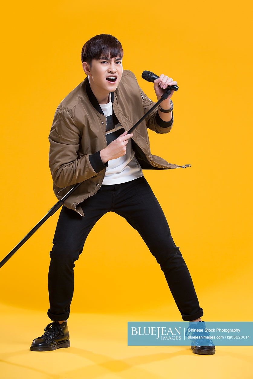 Cheerful young Chinese man singing with microphone-High-res stock photo for download