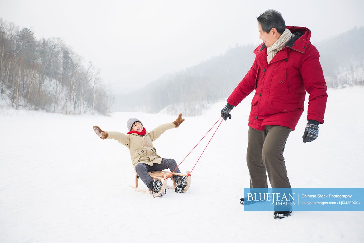 Chinese grandfather pulling grandson on sled-High-res stock photo for download