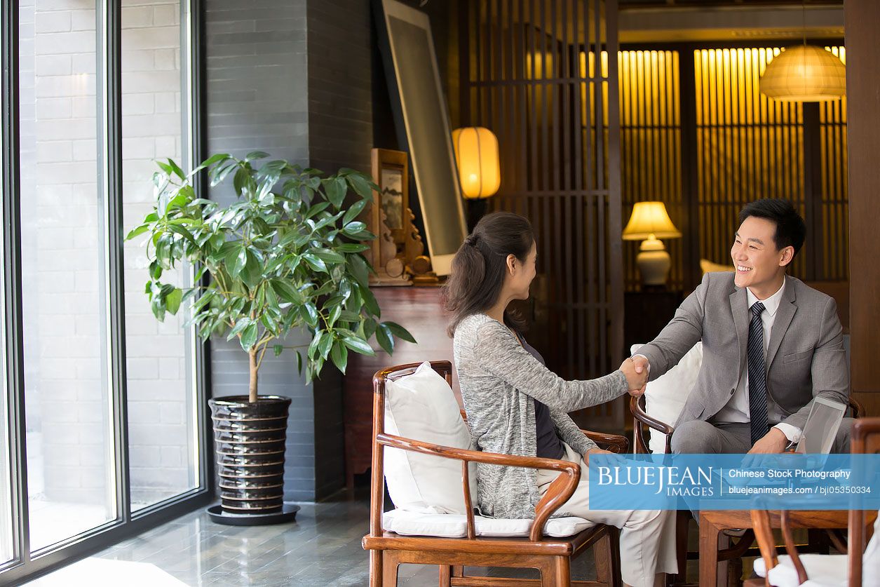 Confident Chinese financial consultant shaking hands with mature woman ...