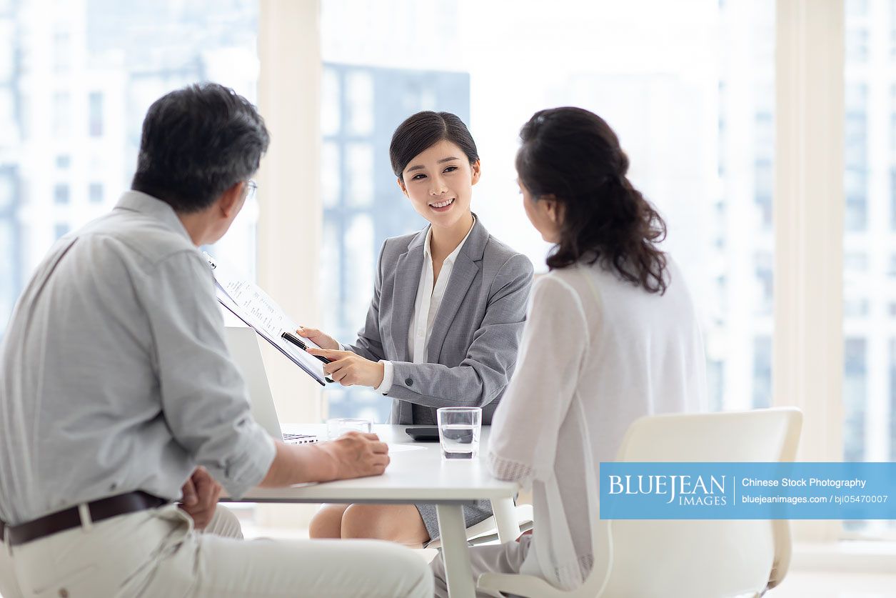Happy mature Chinese couple talking with financial advisor at office ...