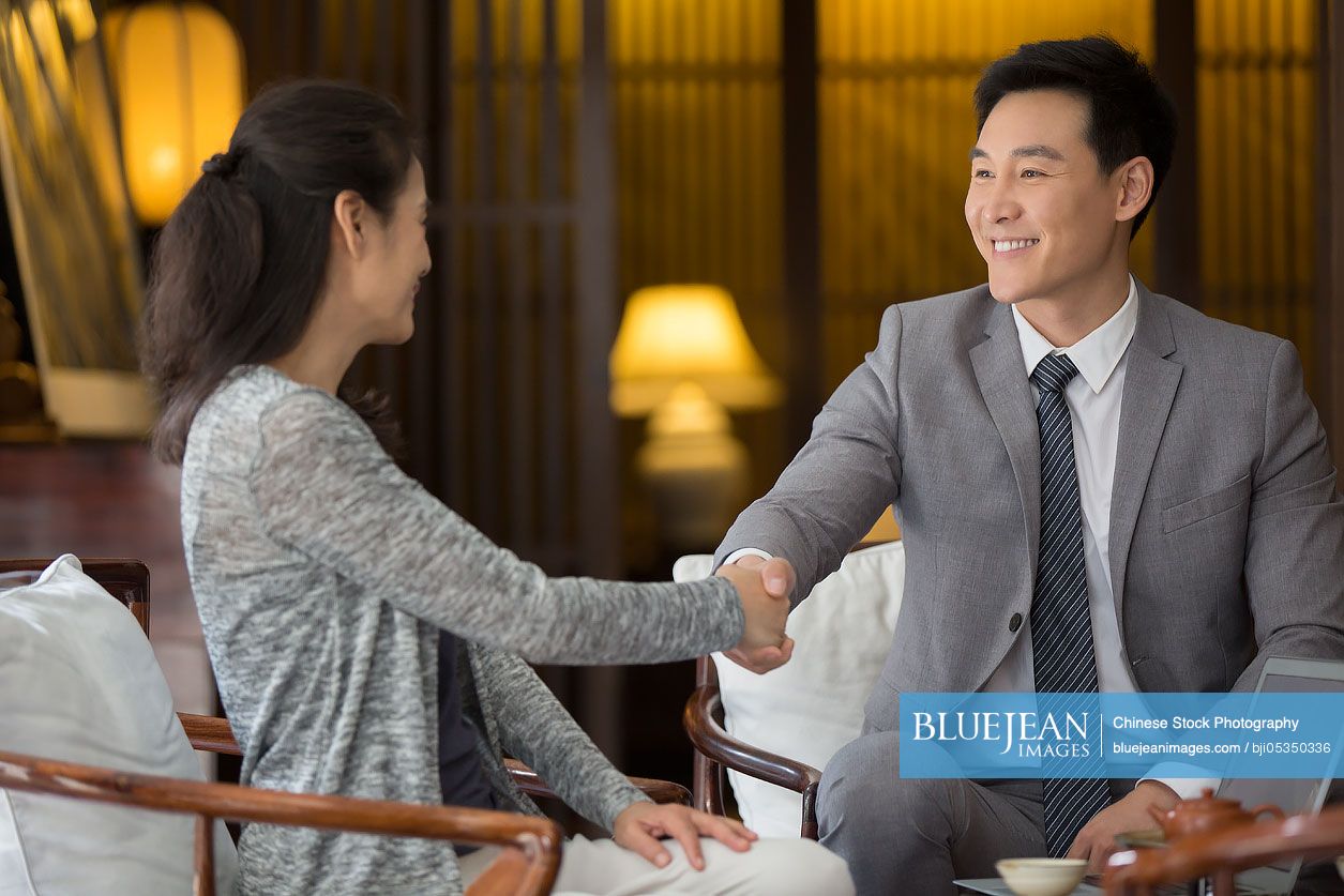 Confident Chinese financial consultant shaking hands with mature woman ...