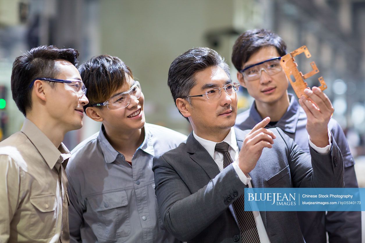 Chinese businessman and engineers checking machine parts in the factory ...