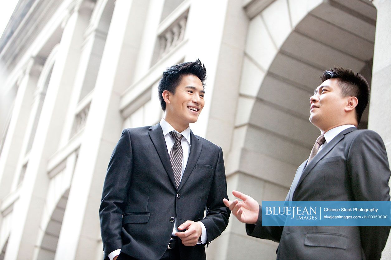 Cheerful Chinese businessmen chatting in front a building, Hong Kong ...