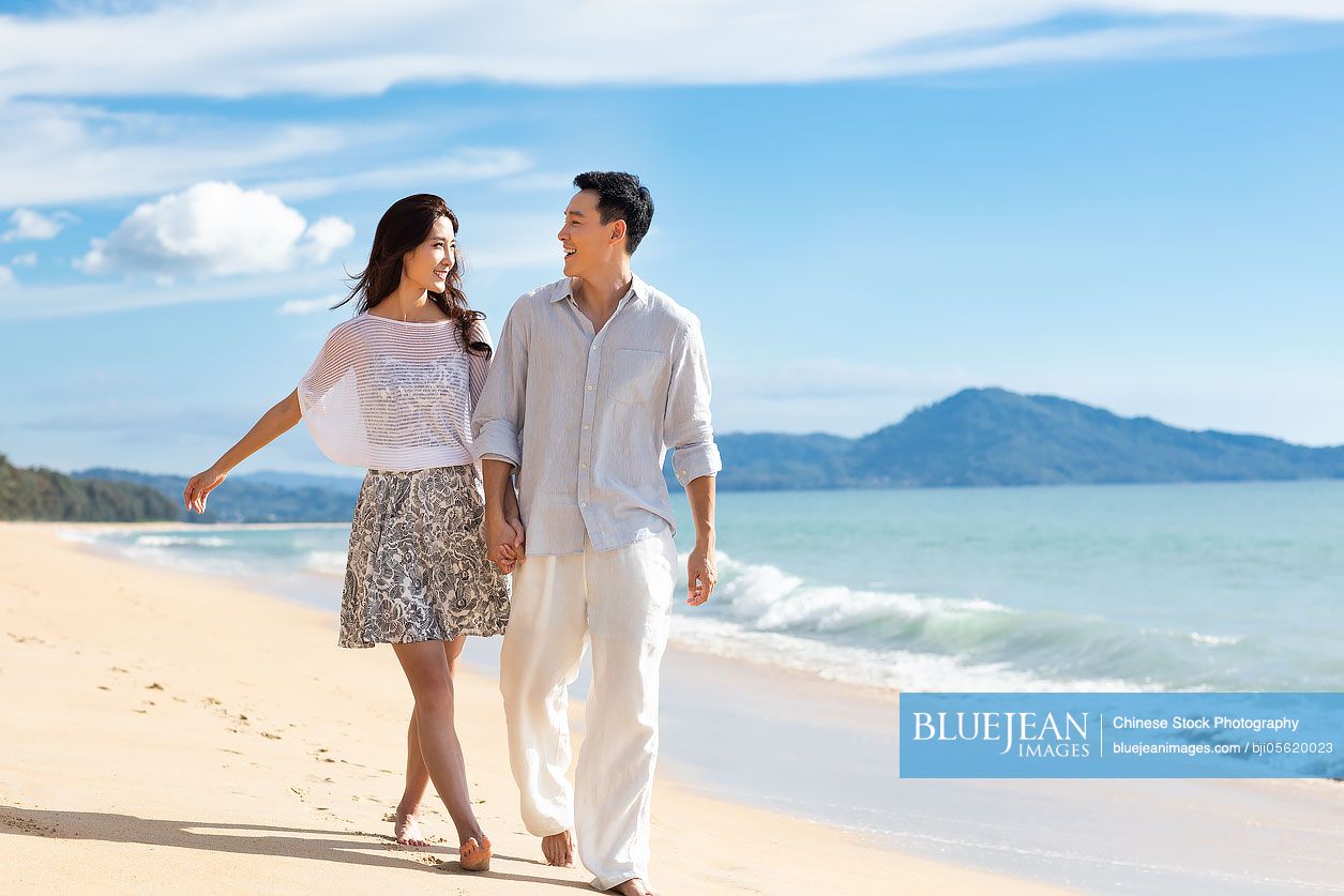 Happy young Chinese couple walking on beach-High-res stock photo for download