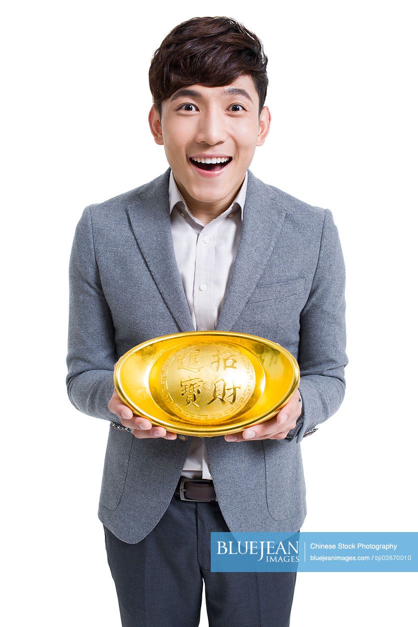 Happy young Chinese man holding a large traditional currency yuanbao ...