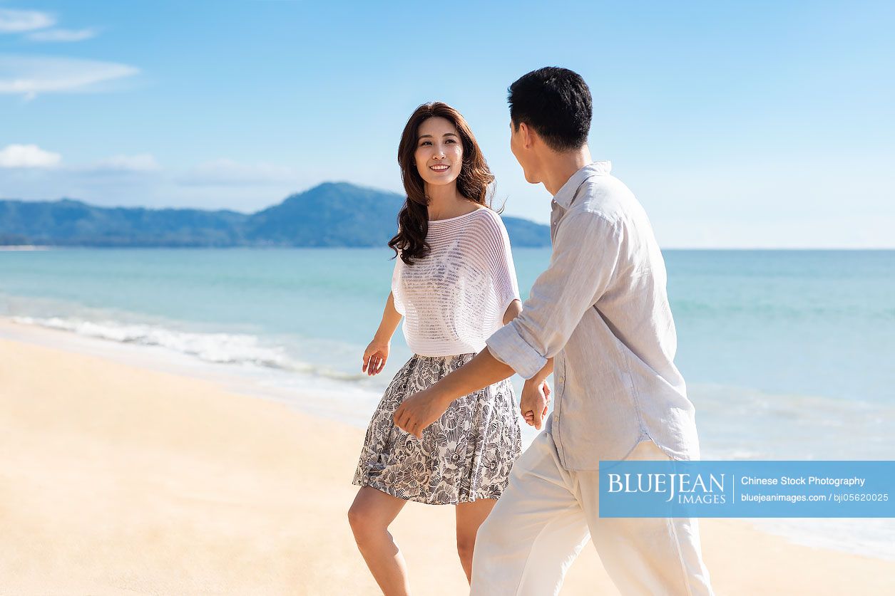 Happy young Chinese couple walking on beach-High-res stock photo for download