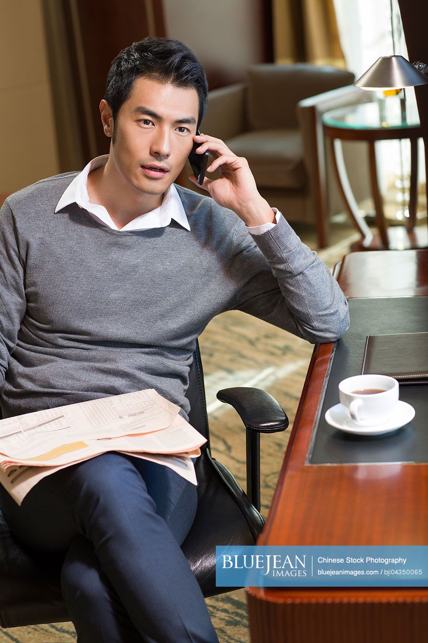 Young Chinese businessman reading newspaper and talking on phone-High ...