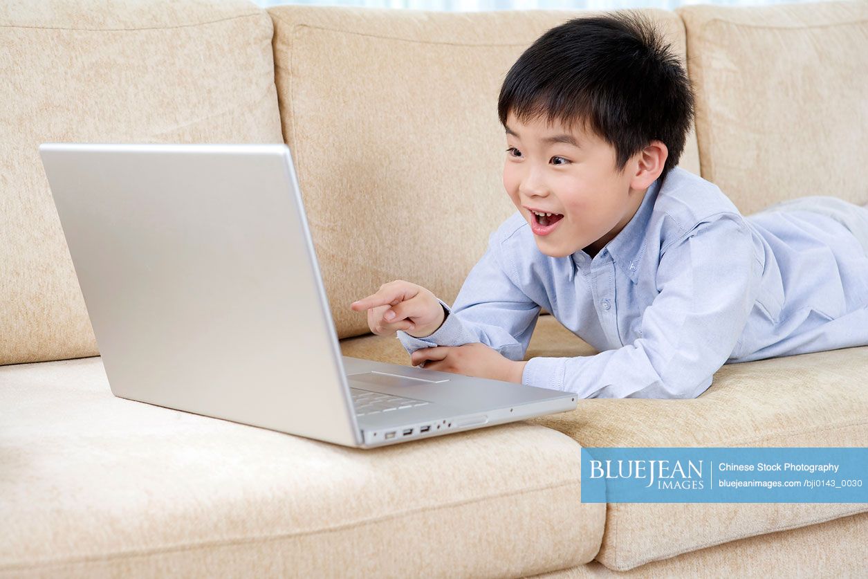 Young Chinese boy pointing at laptop screen on sofa-High-res stock ...