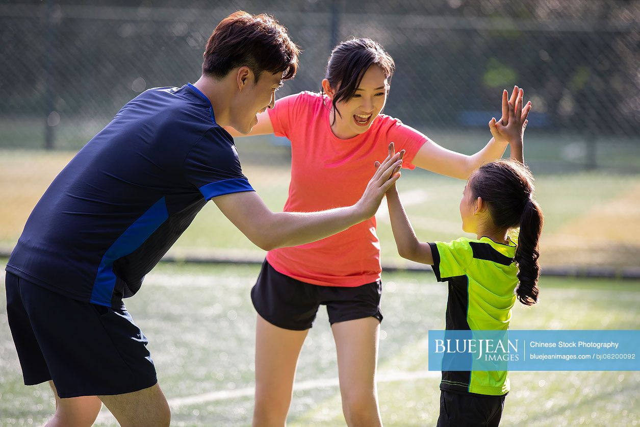 Happy young Chinese family playing football on soccer field-High-res stock photo for download