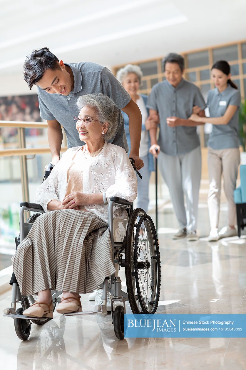 Young Chinese nurse assistant taking care of senior woman in wheelchair ...