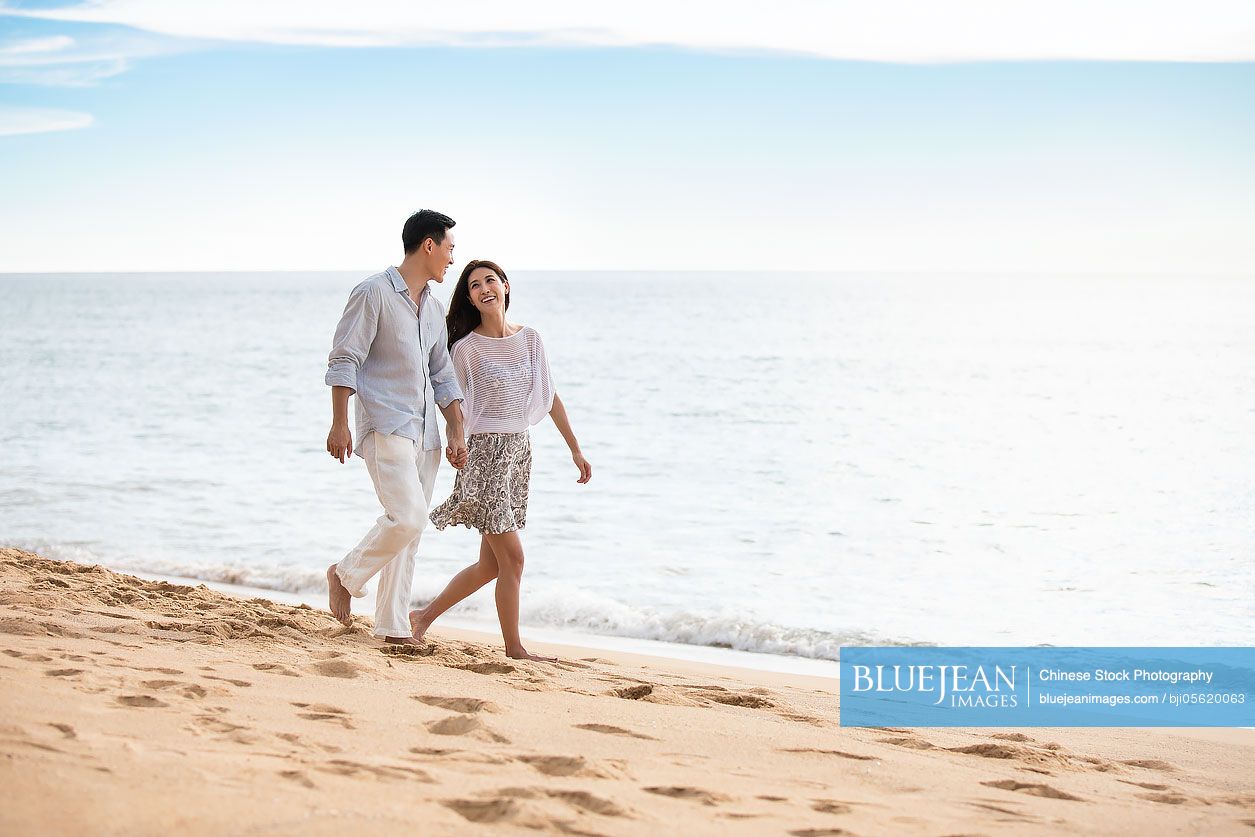 Happy young Chinese couple walking on beach-High-res stock photo for download