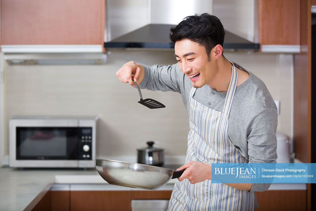 Cheerful Chinese young man doing taste test in kitchen-High-res stock ...