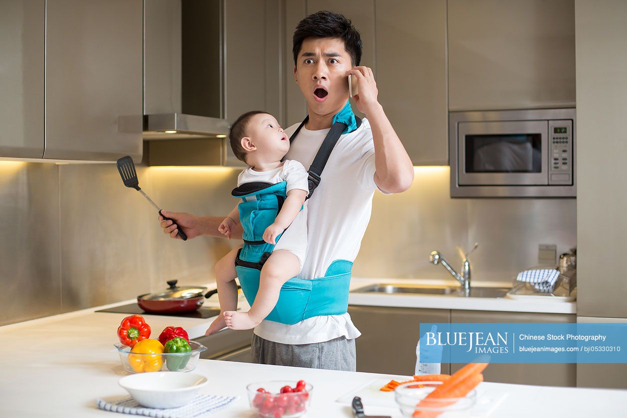 Chinese father holding baby and talking on the phone in kitchen-High ...