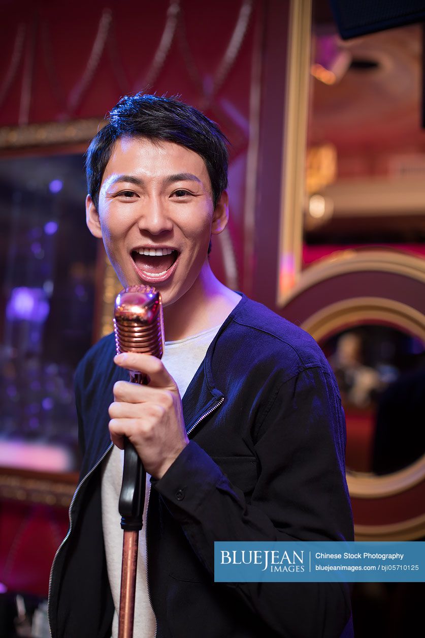 Happy young Chinese man singing karaoke in nightclub-High-res stock photo for download