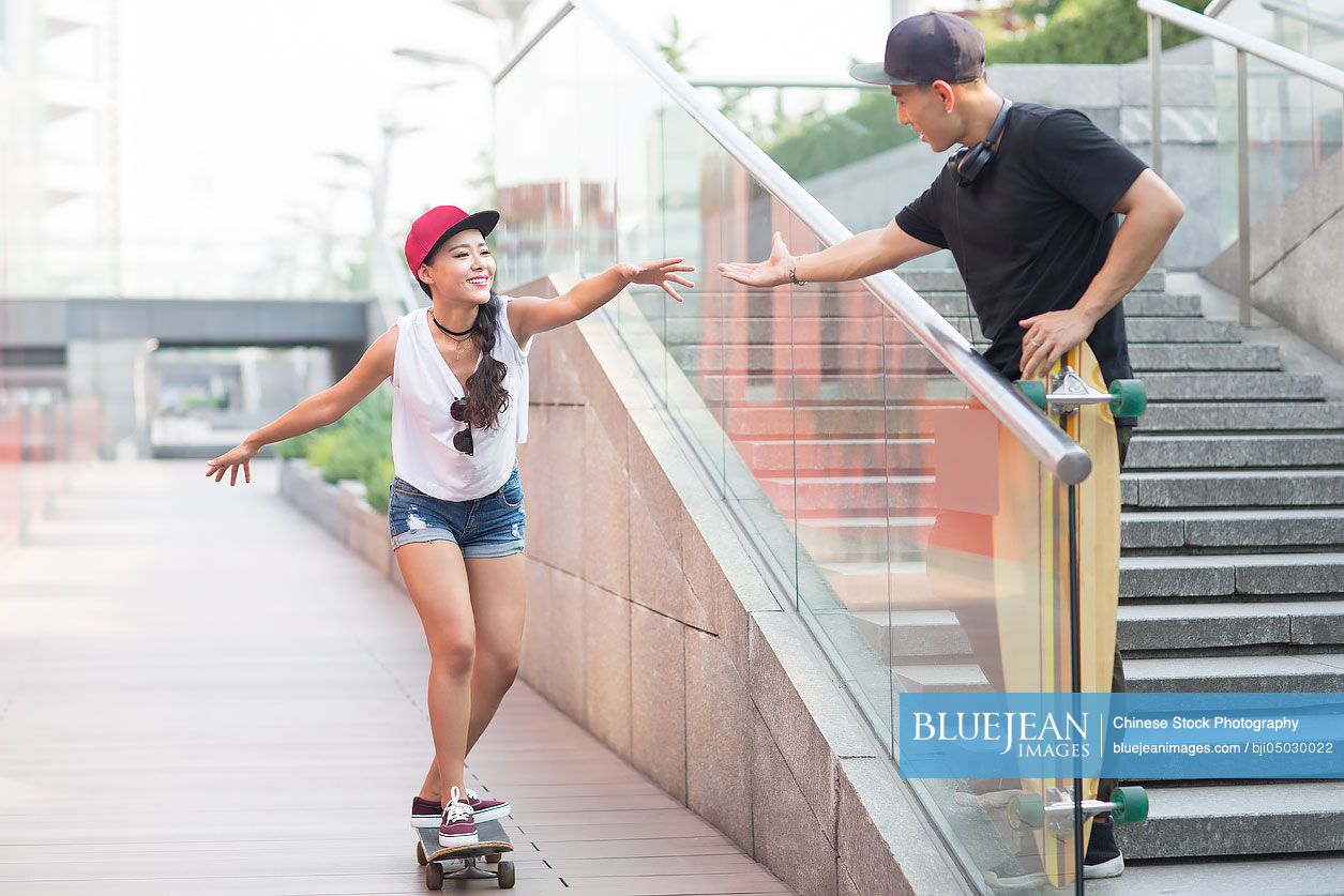 Cheerful young Chinese couple skateboarding-High-res stock photo for ...