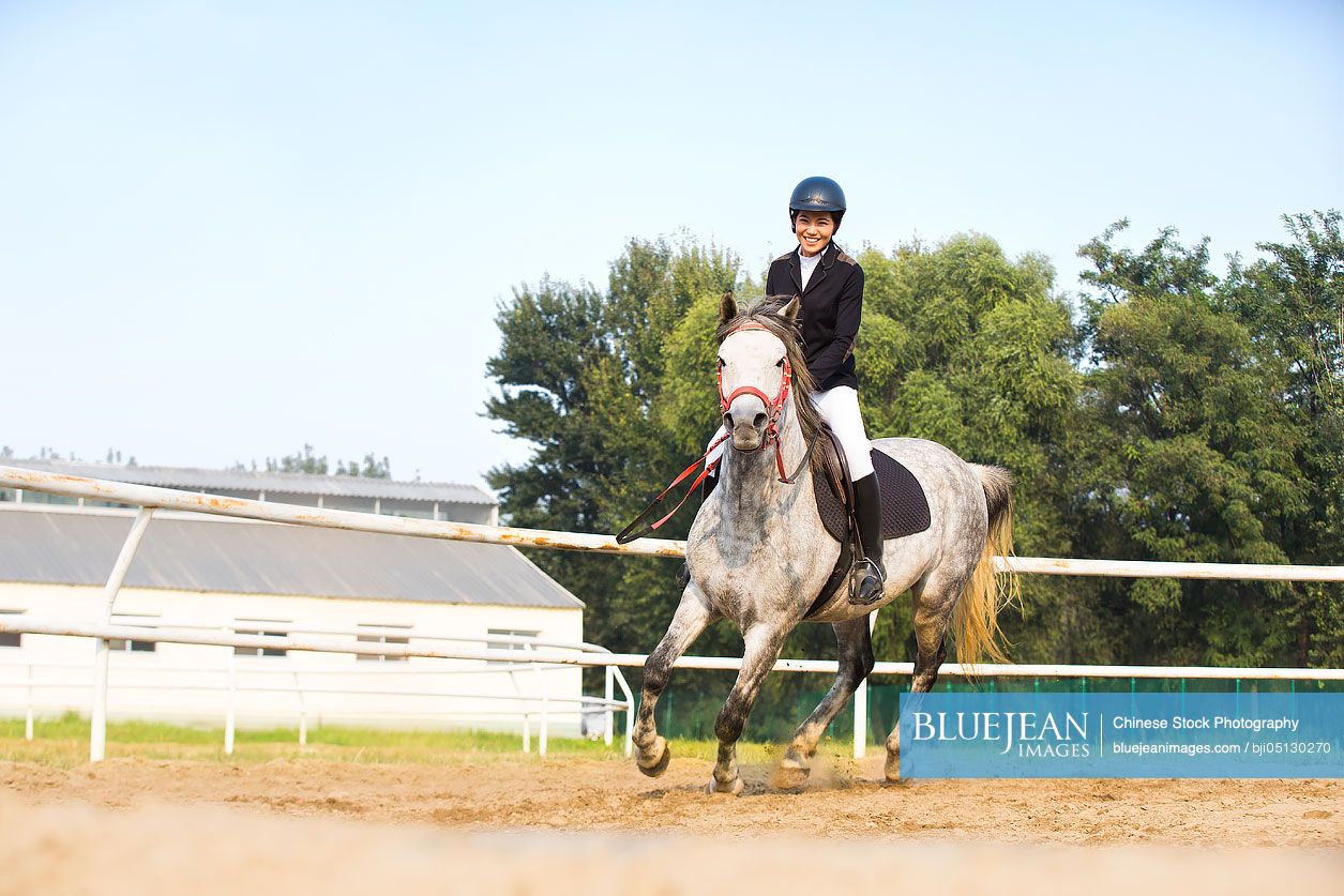Cheerful young Chinese woman riding horse-High-res stock photo for download