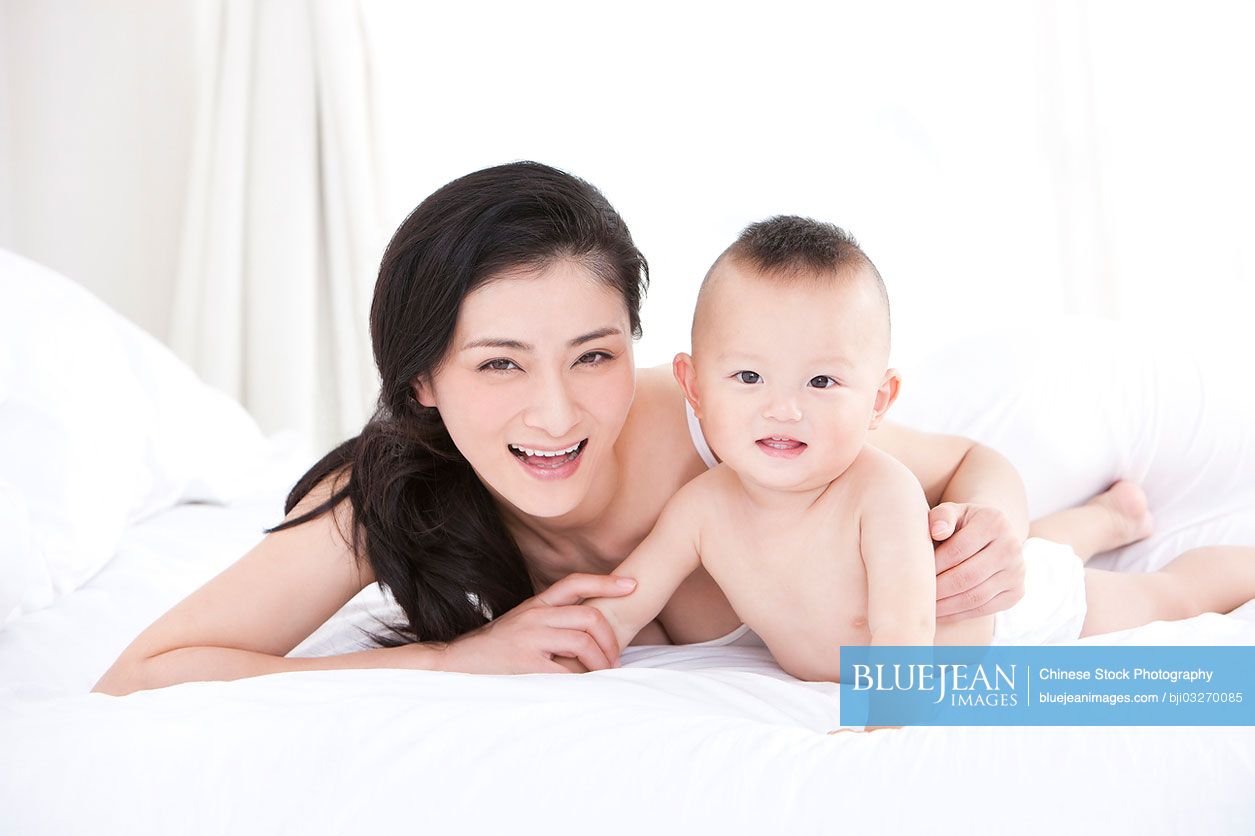 Chinese Mother And Baby Boy Smiling In Bedroom High Res Stock Photo For