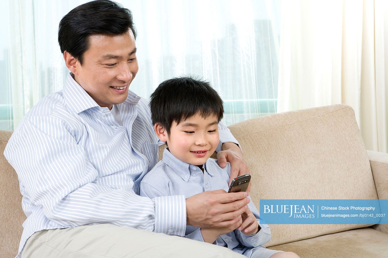 Chinese father and son using cell phone or PDA on sofa-High-res stock ...
