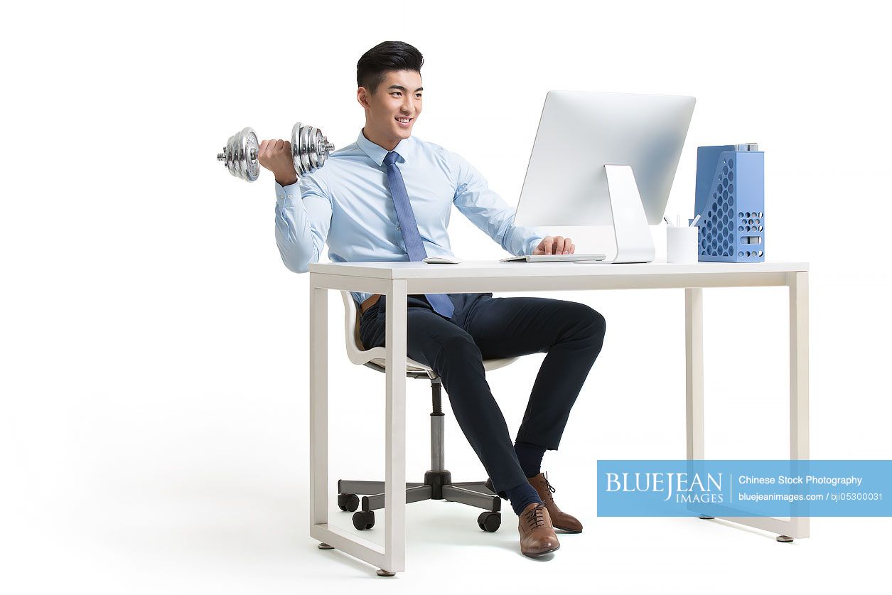 Young Chinese businessman lifting weights while using computer at work-High-res stock photo for ...