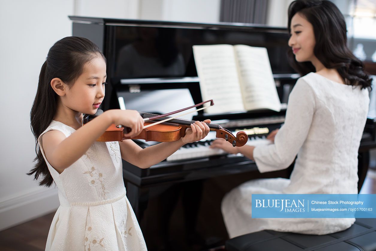 Chinese mother and daughter playing the piano and violin together-High ...