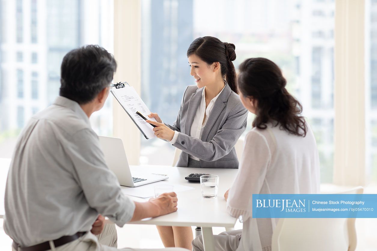 Happy mature Chinese couple talking with financial advisor at office ...