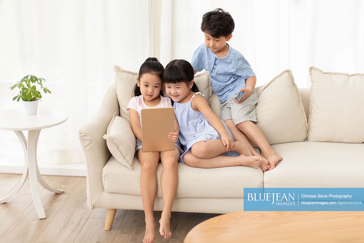 Cute Chinese children using digital tablet on sofa-High-res stock photo for download