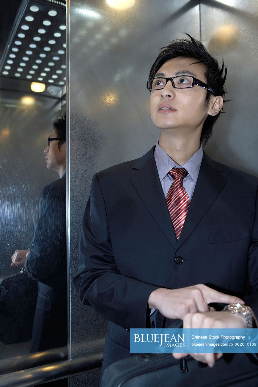 Chinese man looking at watch in elevator-High-res stock photo for download
