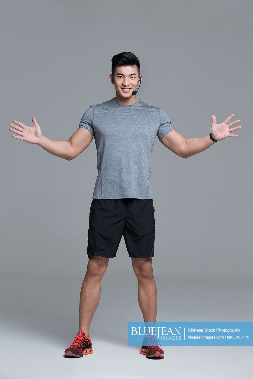 Cheerful young Chinese male trainer with headset teaching at gym-High ...
